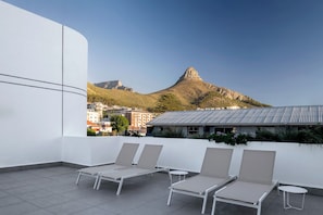 Terraço no telhado com espreguiçadeiras e vista para uma montanha.