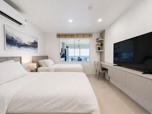 Quarto de hotel moderno com duas camas, uma escrivaninha, televisão e uma grande janela com vista.