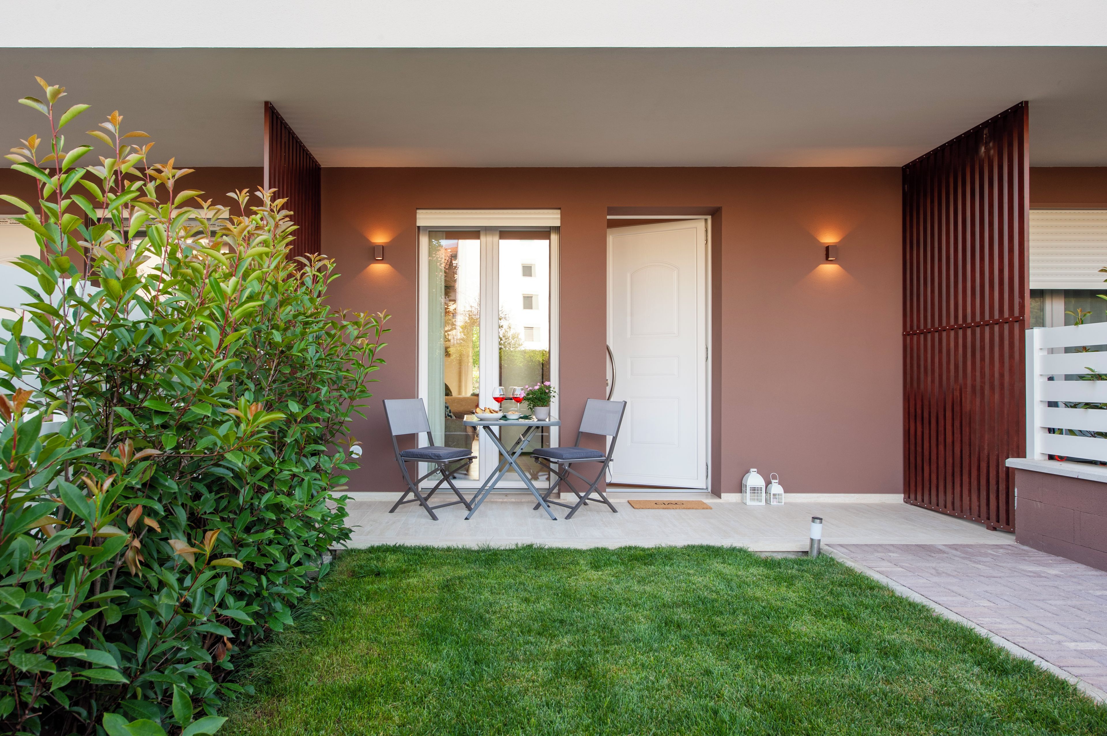 Um pátio moderno ao ar livre com uma mesa e cadeiras de jantar, uma pequena área de jardim e uma porta de correr que dá para uma varanda.