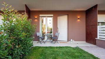 Um pátio moderno ao ar livre com uma mesa e cadeiras de jantar, uma pequena área de jardim e uma porta de correr que dá para uma varanda.
