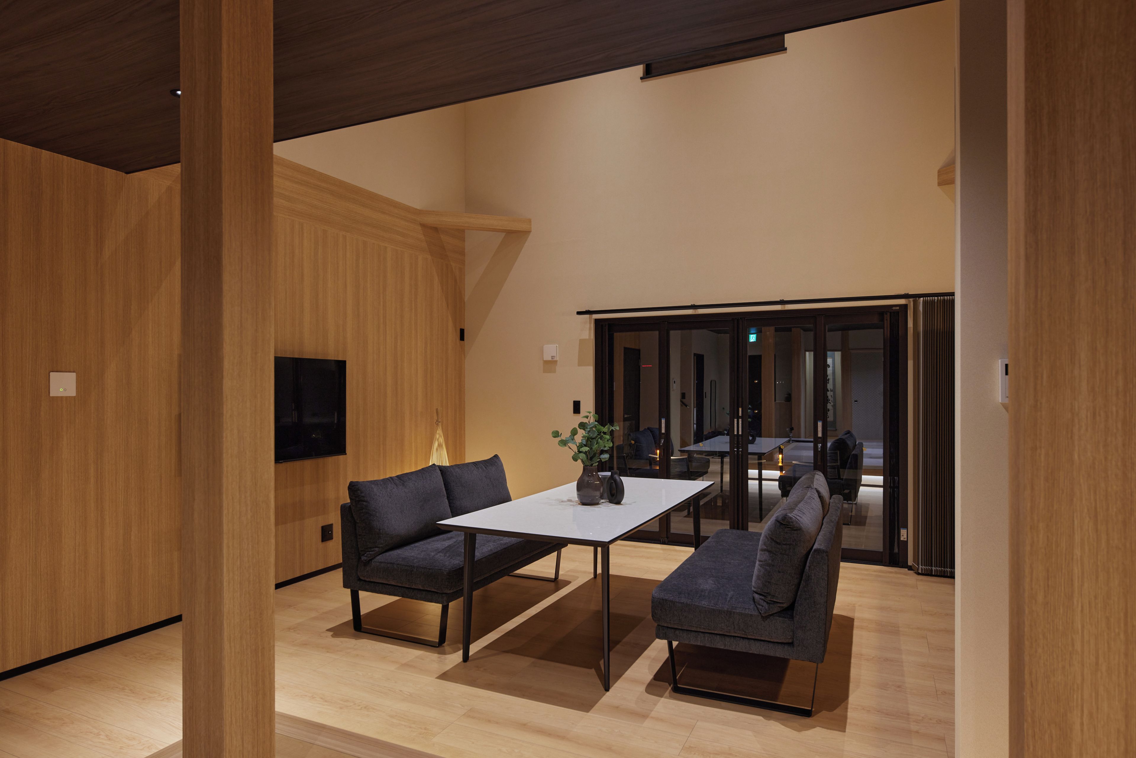 Um interior moderno com parede de destaque em madeira, televisão de tela plana, mesa com cadeiras e porta de vidro que dá para outro cômodo.