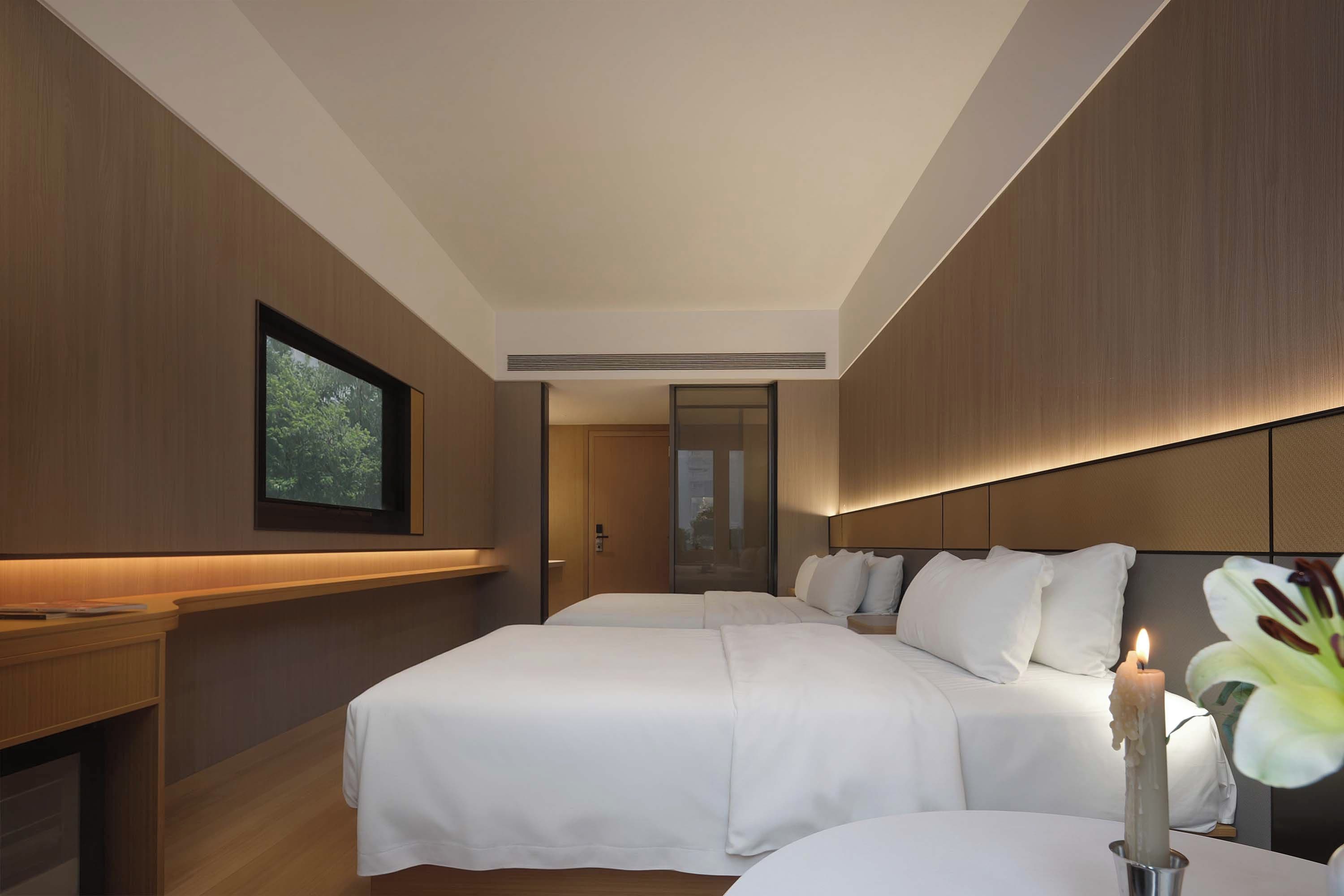 Quarto de hotel com cama, mesa de cabeceira e uma janela ampla.