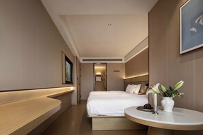Quarto de hotel moderno com cama, mesa de cabeceira e uma pequena mesa redonda com um vaso de flores.