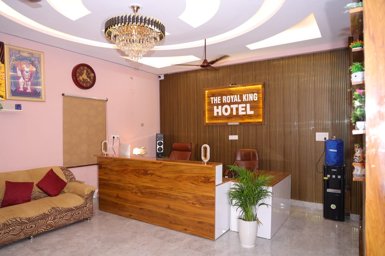 Uma área de recepção com uma mesa de madeira, um sofá, um candelabro e uma placa com a inscrição 'The Royal King Hotel'.