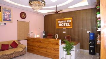 Uma área de recepção com uma mesa de madeira, um sofá, um candelabro e uma placa com a inscrição 'The Royal King Hotel'.