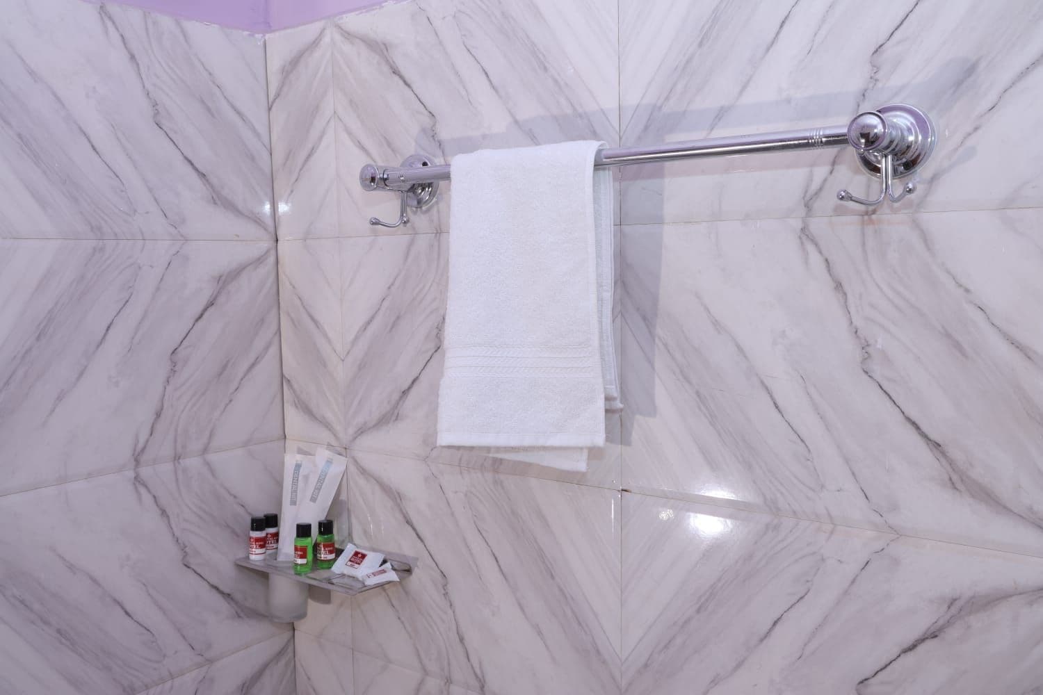 Casa de banho com parede de mármore, um porta-toalhas com toalha branca e um armário com artigos de higiene pessoal.