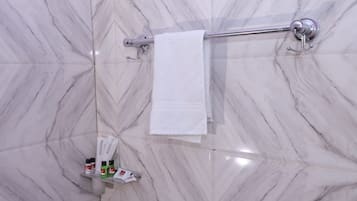 Casa de banho com parede de mármore, um porta-toalhas com toalha branca e um armário com artigos de higiene pessoal.