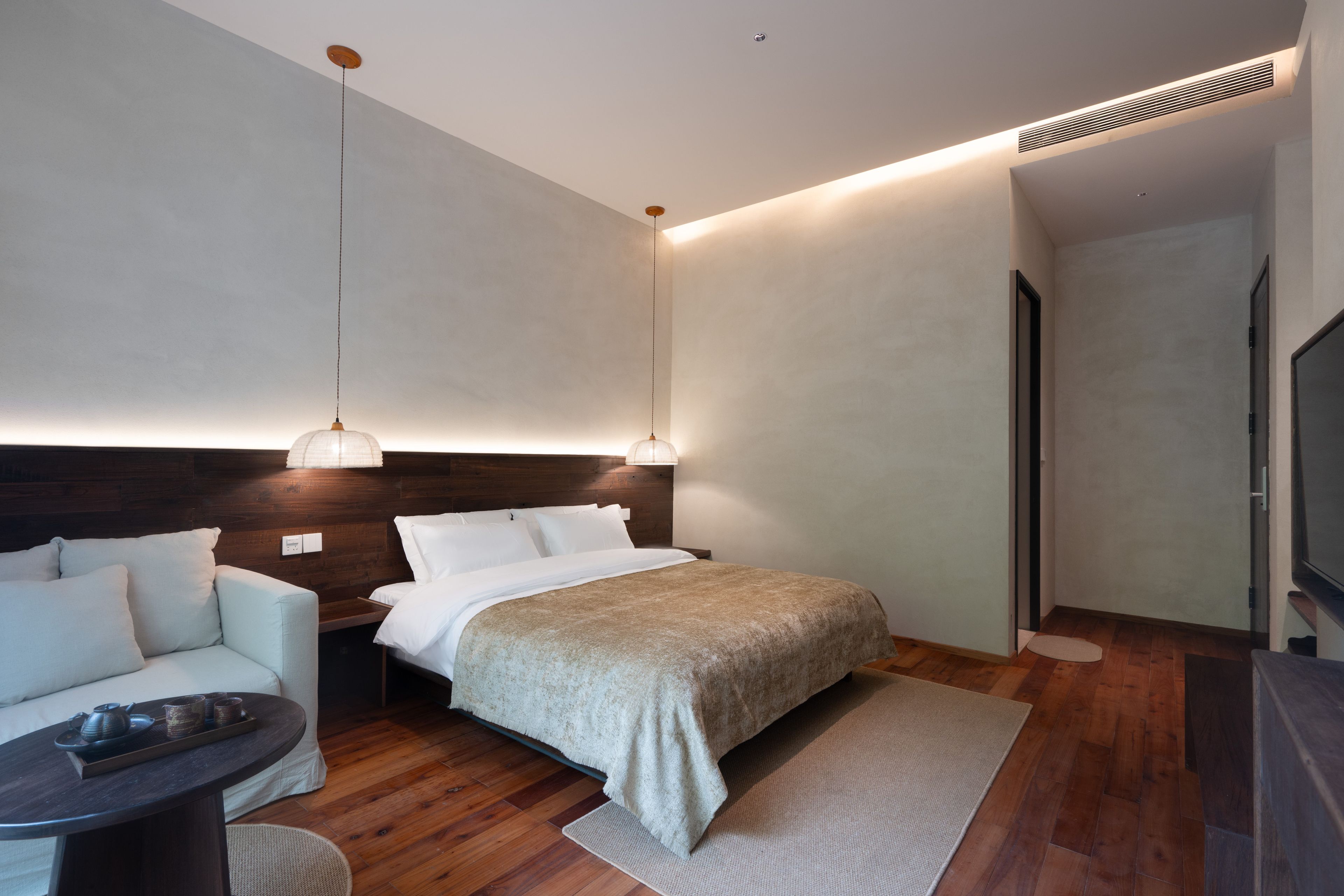 Quarto moderno com cama, mesas de cabeceira, um sofá, TV e piso de madeira.