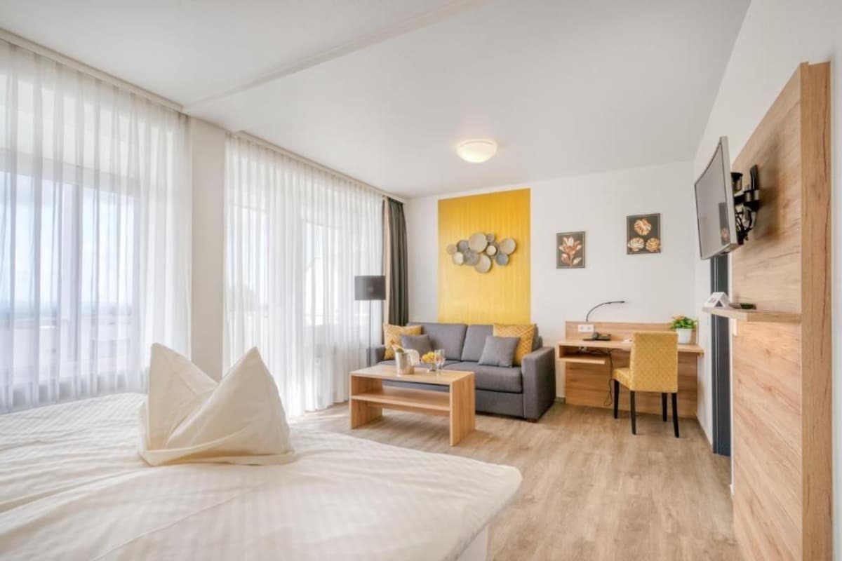 Quarto de hotel com cama, sofá, escrivaninha e televisão.