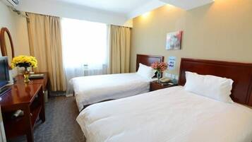 Quarto de hotel com duas camas de solteiro, uma escrivaninha com computador, uma cadeira e uma janela com cortinas.