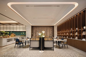 Um saguão de hotel moderno com uma área de estar central, uma cozinha ao fundo e uma parede de madeira com prateleiras embutidas.