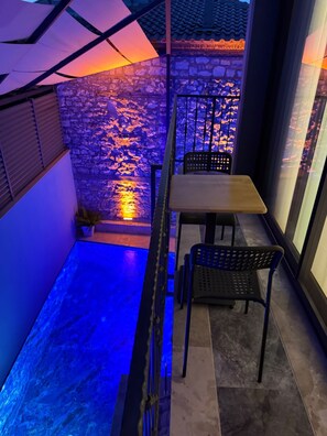 Um espaço exterior estreito com parede de pedra, uma mesa pequena e duas cadeiras.