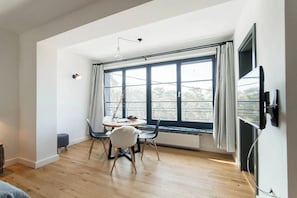 Quarto moderno com uma janela grande, uma mesa de jantar com cadeiras e uma televisão de tela plana na parede.