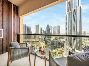 Uma varanda com vista para a cidade, uma mesa com um copo de suco e duas cadeiras.