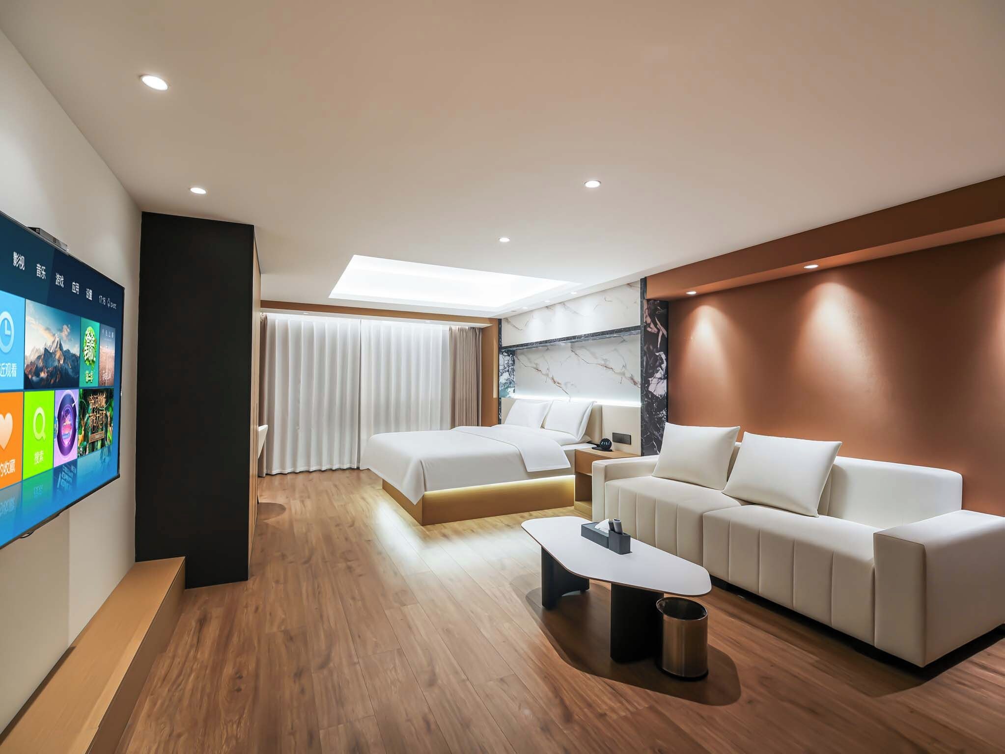 Quarto de hotel moderno com cama, sofá, televisão e claraboia.