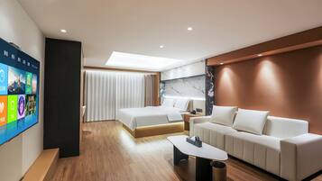 Quarto de hotel moderno com cama, sofá, televisão e claraboia.