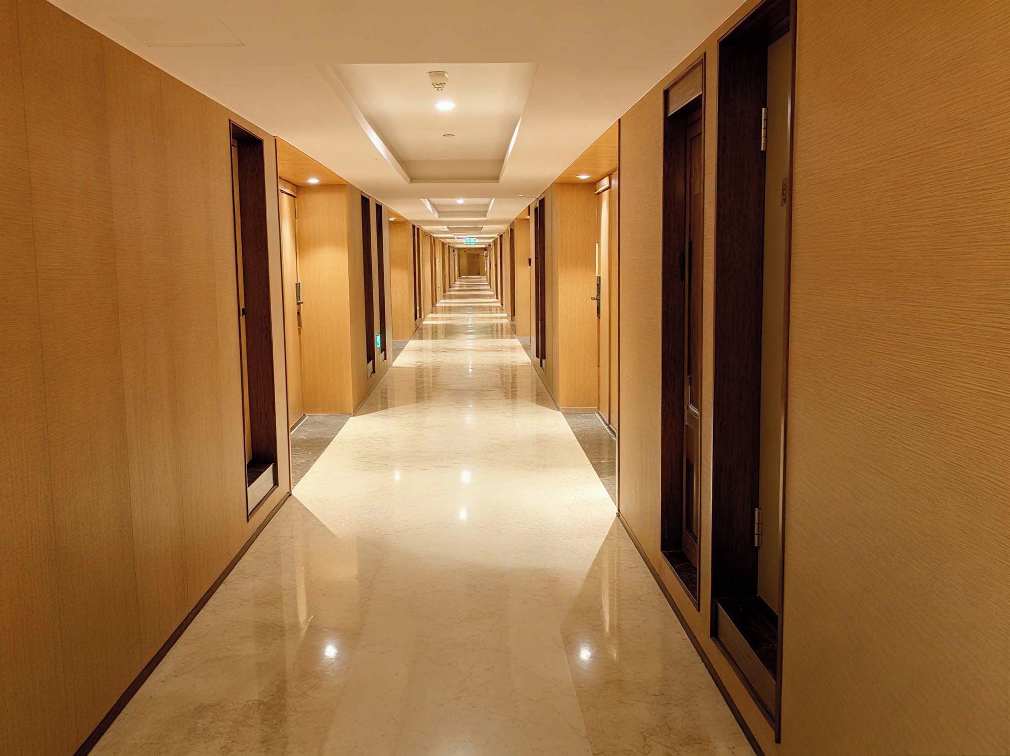 Corredor de hotel com paredes e portas de madeira, piso brilhante e teto com iluminação embutida.