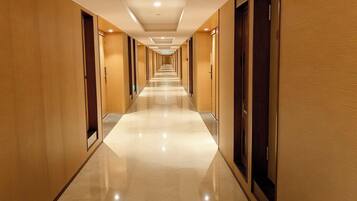 Corredor de hotel com paredes e portas de madeira, piso brilhante e teto com iluminação embutida.
