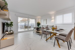 Uma área de jantar moderna com mesa de vidro, cadeiras e vista da cidade por grandes janelas.