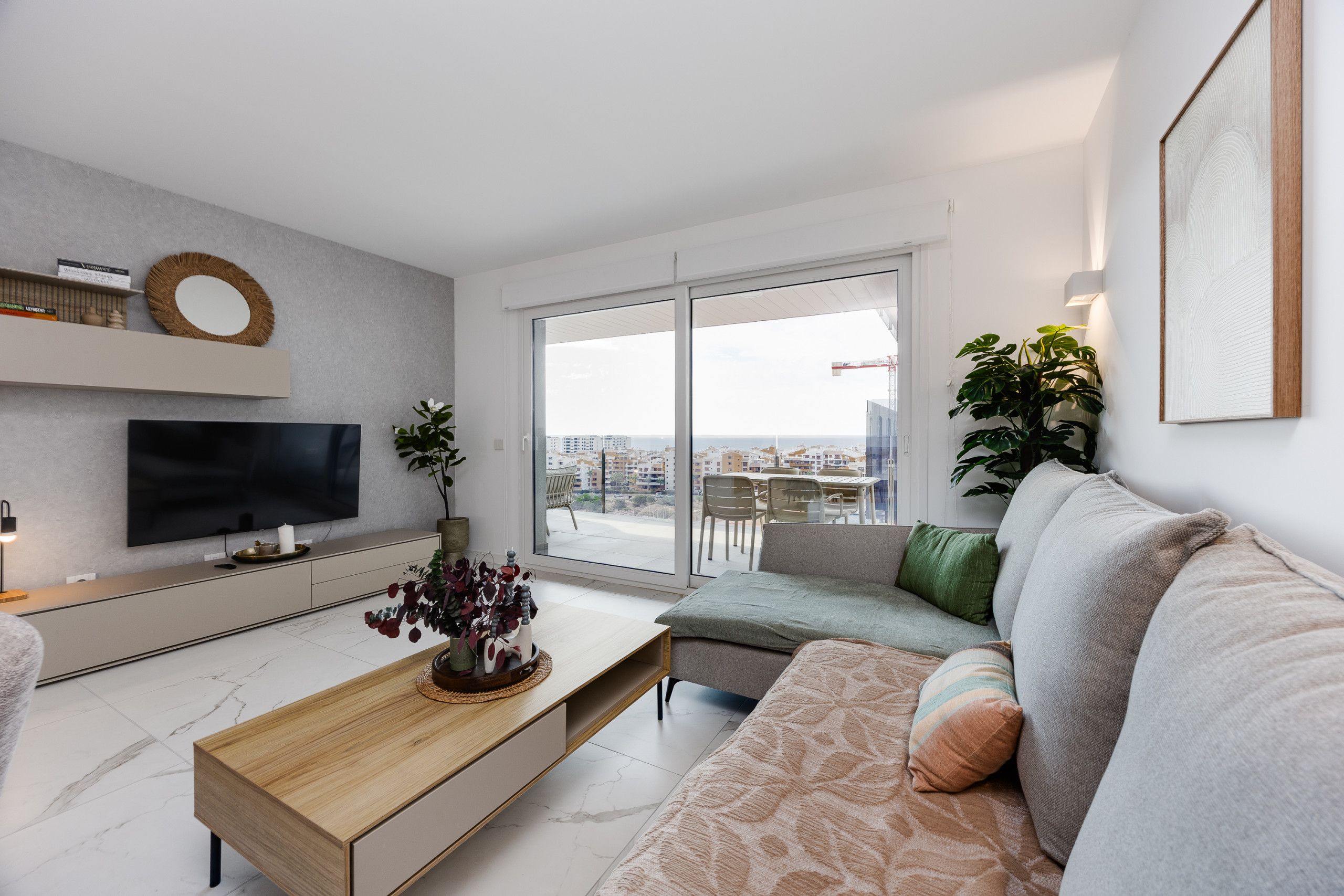 Uma sala de estar moderna com televisão de tela plana, mesa de centro, sofá e uma janela grande com vista para prédios.