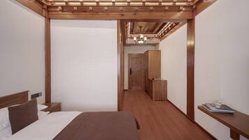 Quarto com cabeceira de madeira, cama com manta marrom, mesa de cabeceira com um livro e um copo, e guarda-roupa de madeira.