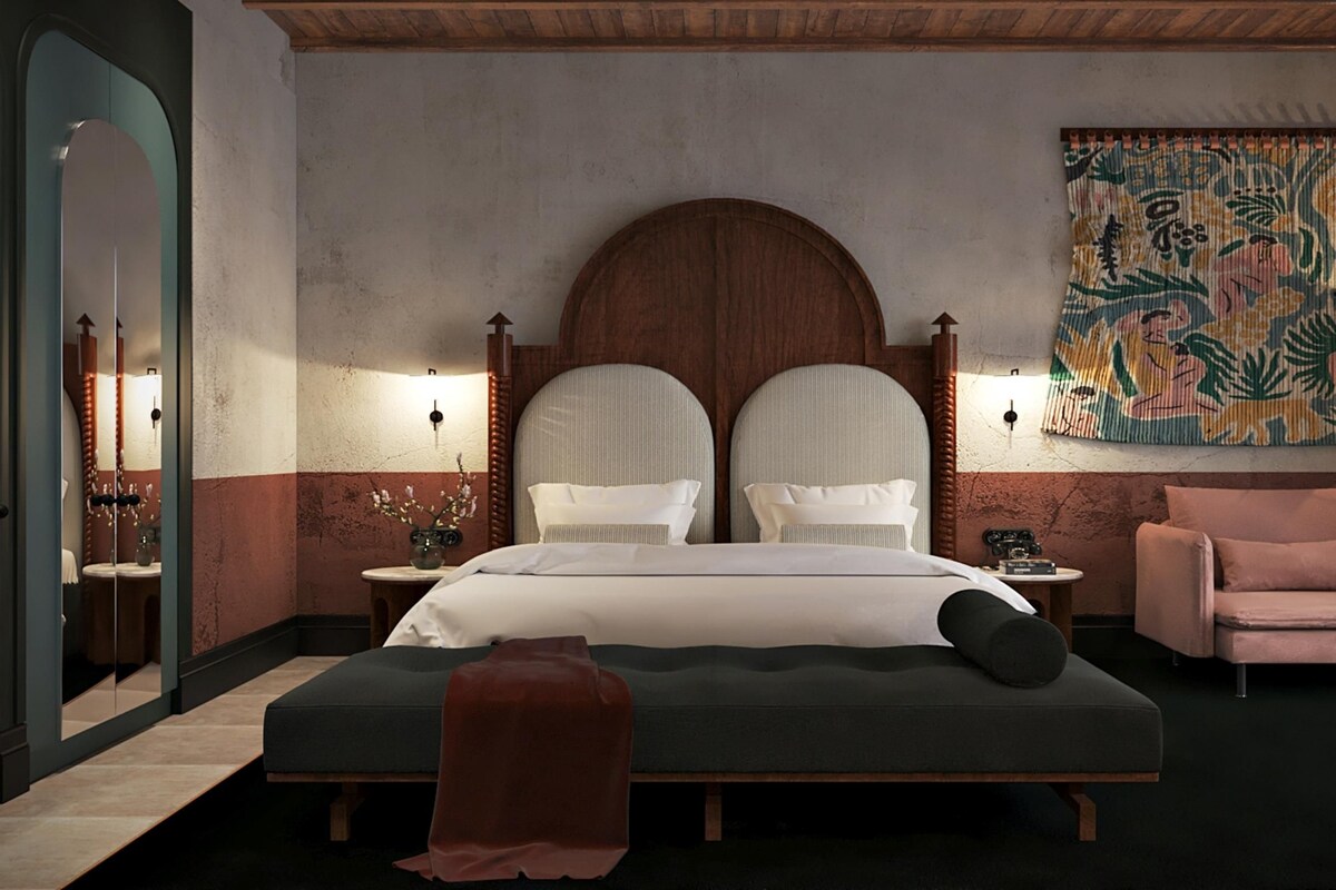 Quarto com cama grande, duas mesas de cabeceira, uma cadeira e uma tapeçaria decorativa.
