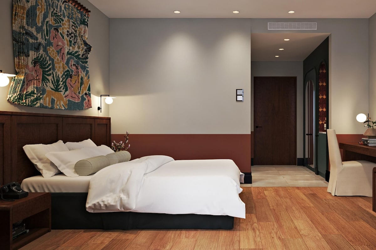 Quarto de hotel com cama, mesa de cabeceira, abajur e televisão.