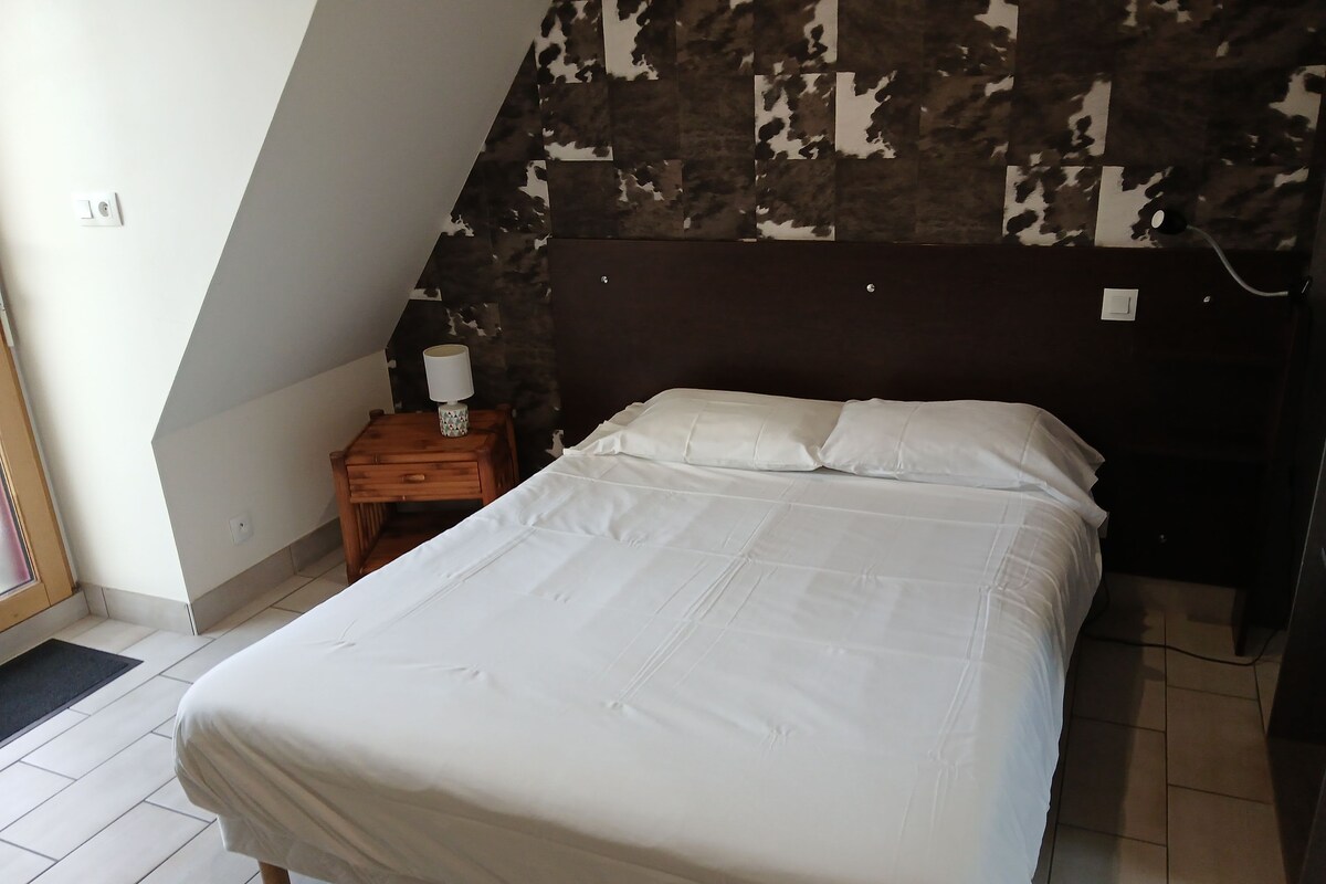 Quarto com cama, mesa de cabeceira, luminária e parede com padrão.