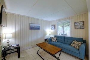 Sala de estar com um sofá azul, uma mesa de centro de madeira, uma luminária e duas pinturas penduradas na parede.