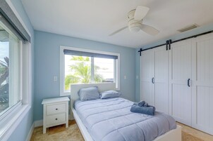 Quarto com cama, mesa de cabeceira, janela com vista para o verde, ventilador de teto e guarda-roupa.