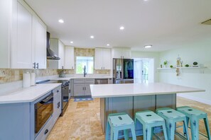 Cozinha moderna com armários brancos, uma ilha central com banquetas e vista para a área de jantar.