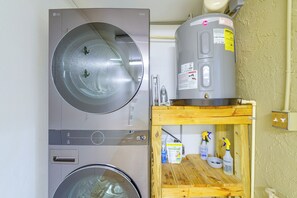Uma área de lavanderia com máquina de lavar, secadora e aquecedor de água, tudo sobre uma prateleira de madeira.