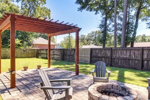 Um pátio nos fundos com pérgola, área de estar externa e lareira.
