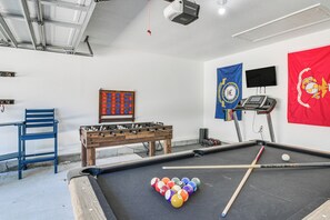 Uma sala de jogos com mesa de bilhar, mesa de pebolim e uma bandeira.