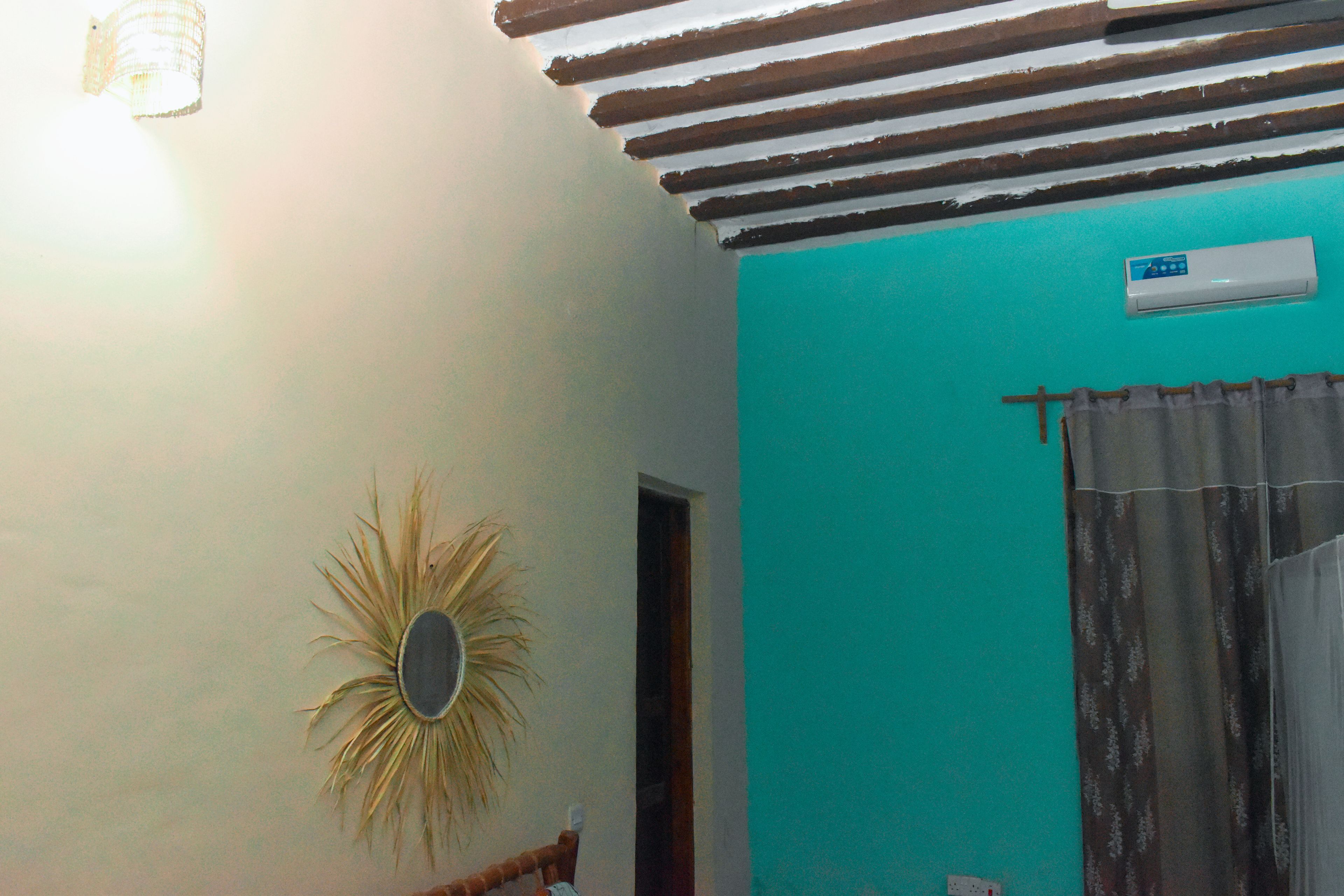 Quarto com parede verde-água, ventoinha de teto, luminária, janela com cortinas e unidade de ar condicionado.