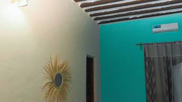 Quarto com parede verde-água, ventoinha de teto, luminária, janela com cortinas e unidade de ar condicionado.