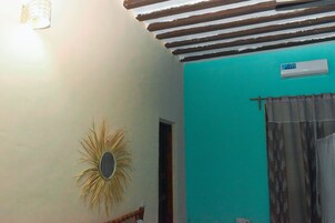 Quarto com parede verde-água, ventoinha de teto, luminária, janela com cortinas e unidade de ar condicionado.