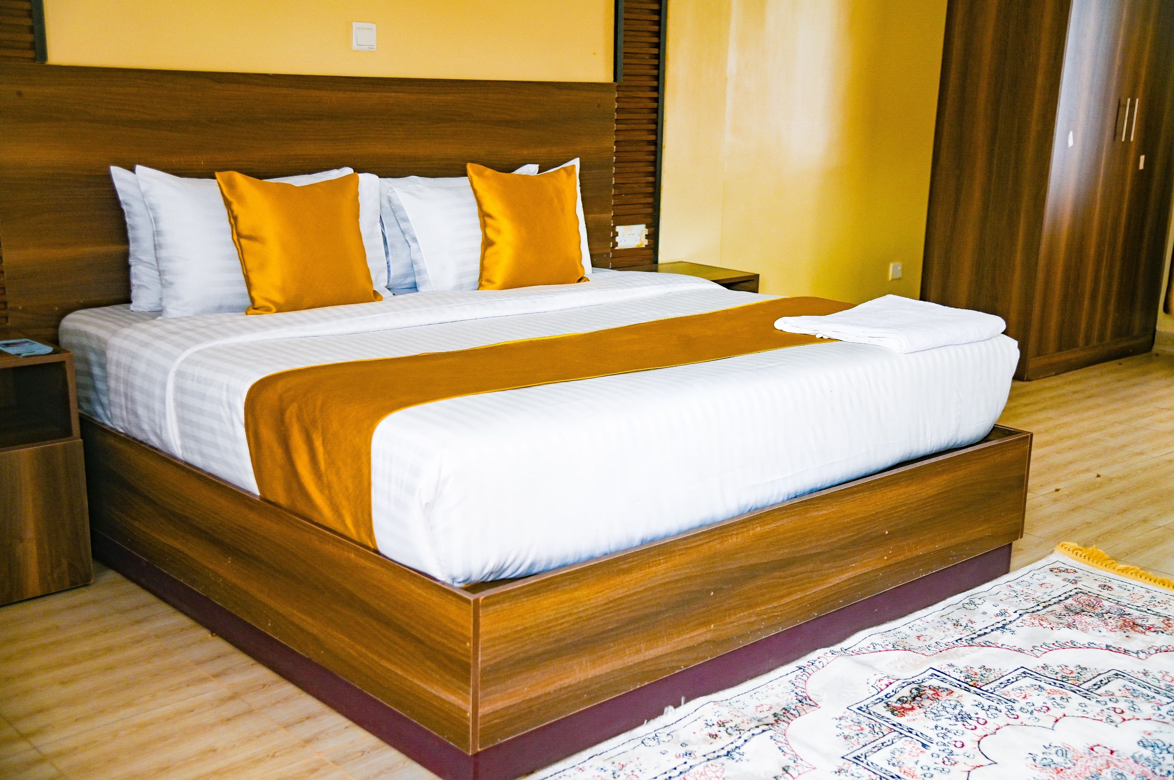 Uma cama grande com estrutura de madeira, roupa de cama branca e duas almofadas amarelas.