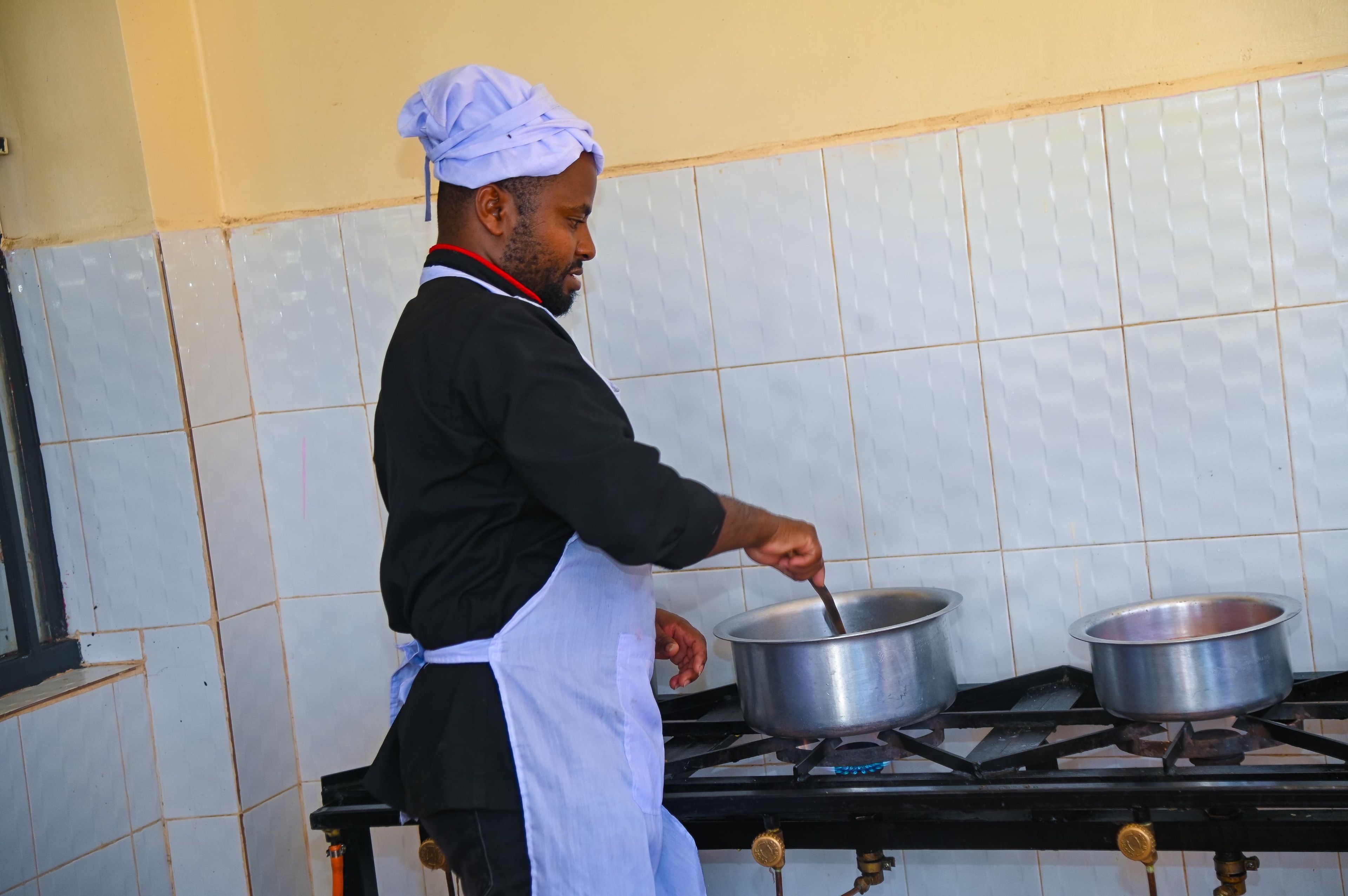 Uma pessoa cozinhando em uma cozinha com fogão a gás e várias panelas.