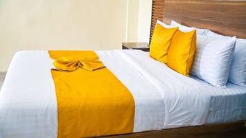 Uma cama com cabeceira de madeira, roupa de cama branca e amarela, e um único travesseiro amarelo.
