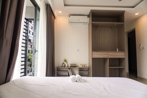Quarto de hotel com cama, guarda-roupa, mesa pequena com um vaso e uma luminária, e janela com cortinas.