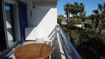 Varanda com mesa e cadeiras de madeira, vista para uma área residencial com palmeiras.