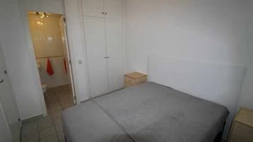 Quarto com cama, guarda-roupa e um pequeno banquinho de madeira.