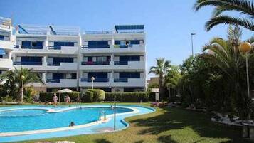 Hotel com vários andares, piscina, palmeiras e vegetação.