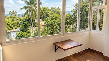Quarto com grandes janelas, um banco de madeira e vista para vegetação e edifícios.