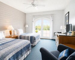 Quarto de hotel com duas camas, uma escrivaninha, uma cadeira, uma televisão e vista para o exterior.