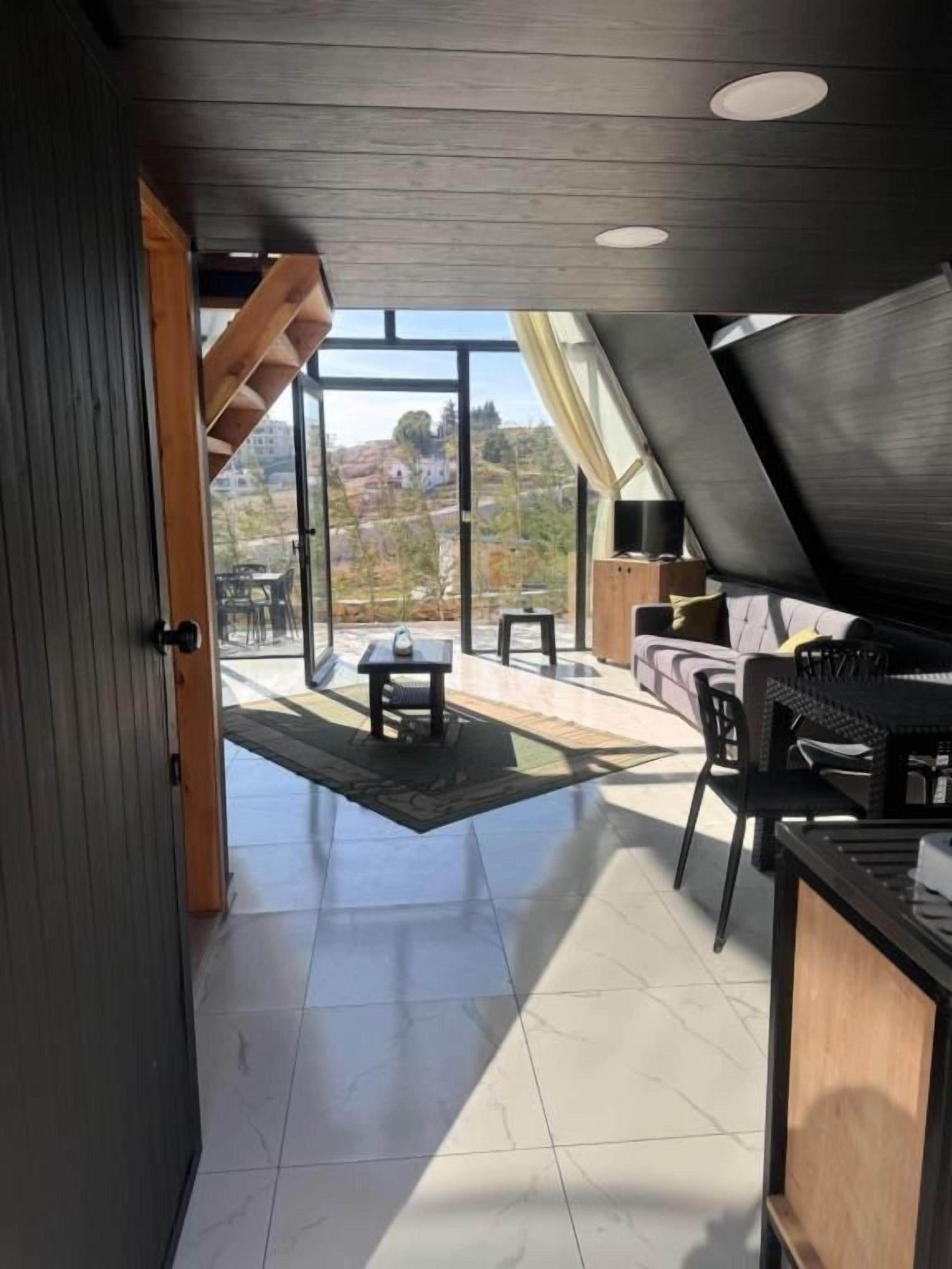 Uma área de estar integrada com vista para uma encosta, uma sala de jantar com mesa e cadeiras, e uma cozinha com bancada e eletrodomésticos.