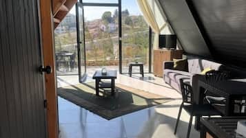 Uma área de estar integrada com vista para uma encosta, uma sala de jantar com mesa e cadeiras, e uma cozinha com bancada e eletrodomésticos.