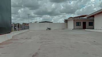 Estacionamento vazio com uma motocicleta, área cercada e um edifício com telhado plano.