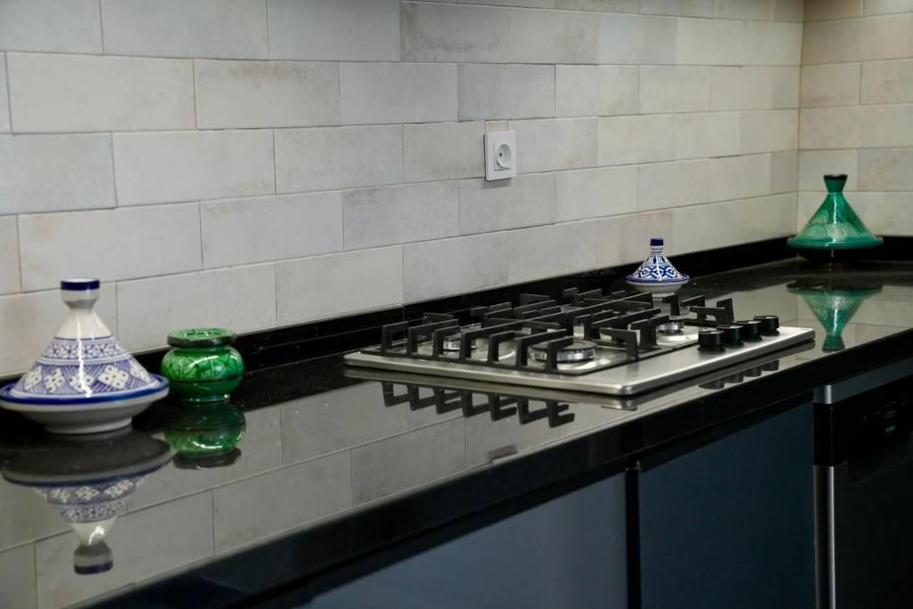 Cozinha com fogão a gás, bancada preta e objetos decorativos, incluindo uma tigela azul e branca e um vaso verde.